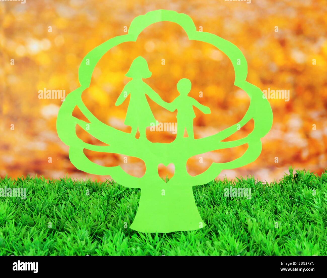 Green cut out paper tree with people inside, on green grass on bright ...