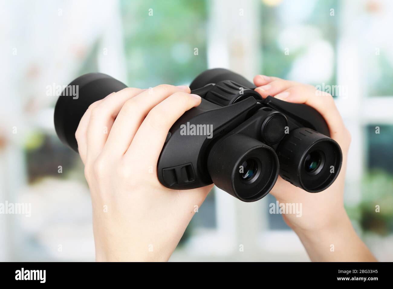 Black modern binoculars in hands on window background Stock Photo - Alamy
