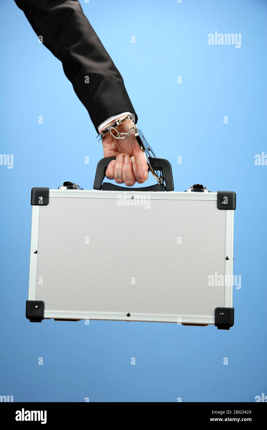 Hand with handcuff and suitcase, on color background Stock Photo - Alamy