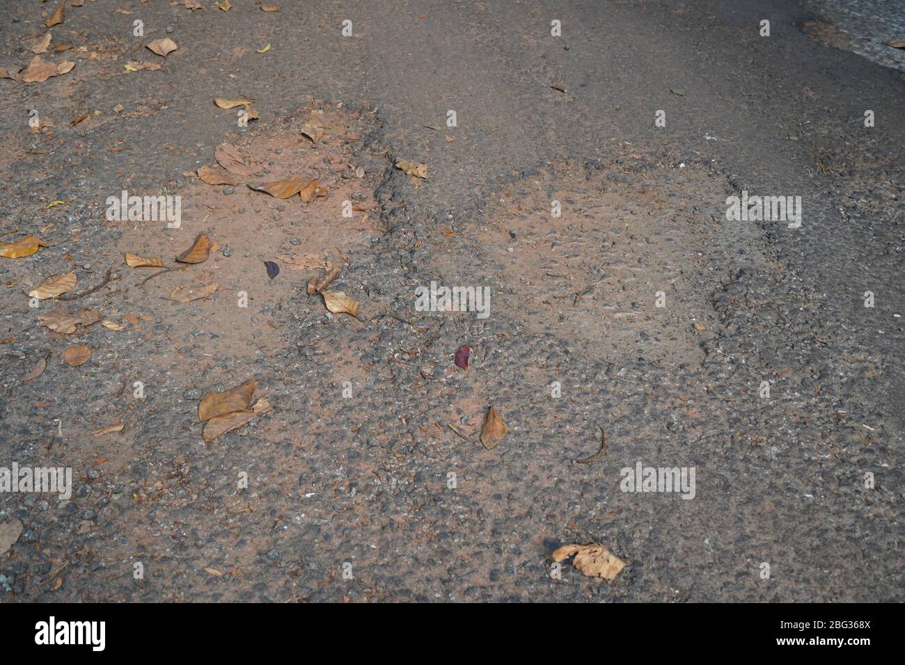 Damaged asphalt pavement road with potholes in rural area. Dry brown ...