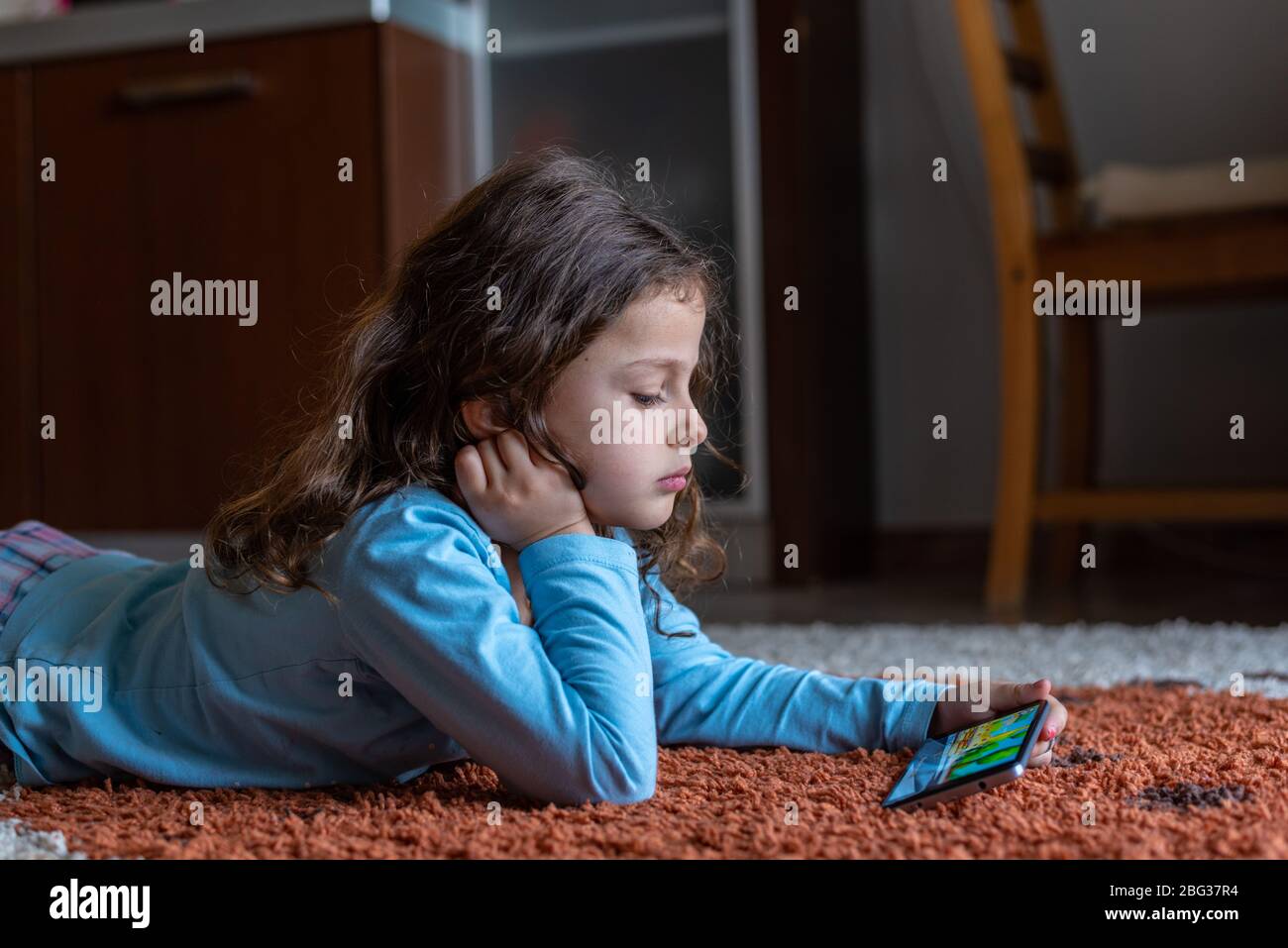 Cute little happy girl lying down on using looking digital smartphone ...