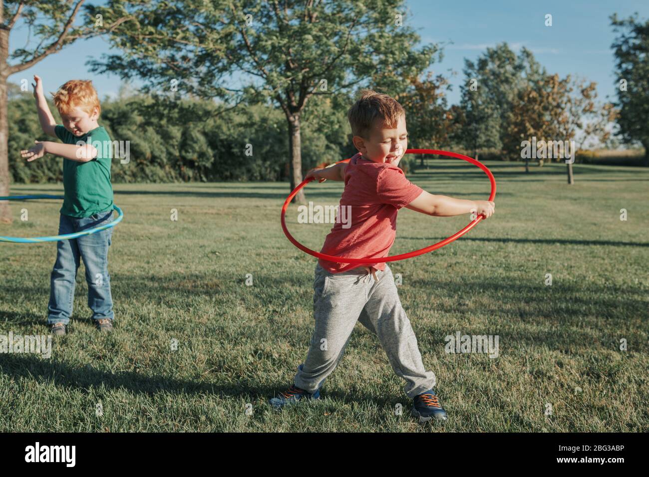 Two funny Caucasian preschool boys playing with hoola hoop in park ...