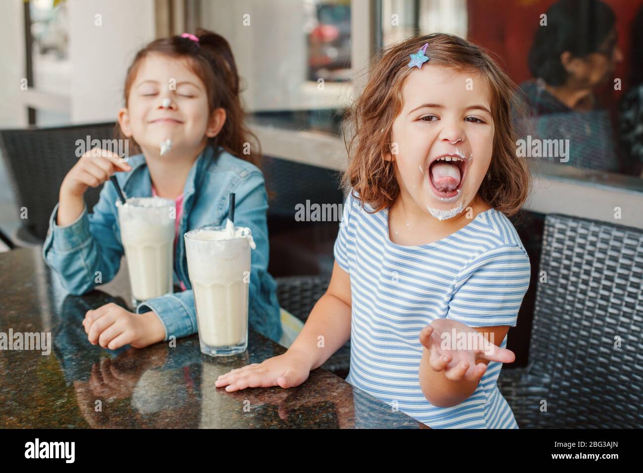 Two funny Caucasian little preschool sisters siblings drink milk shakes ...