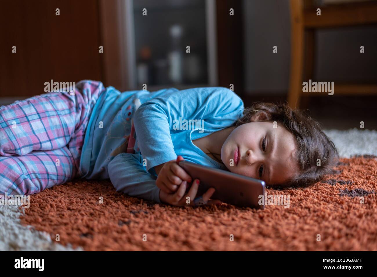 Cute little happy girl lying down on using looking digital smartphone ...