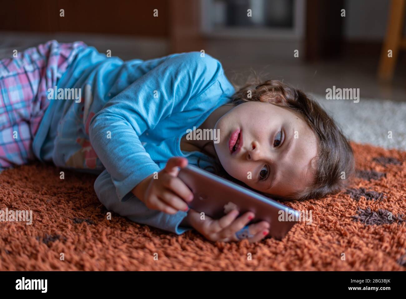 Cute little happy girl lying down on using looking digital smartphone ...