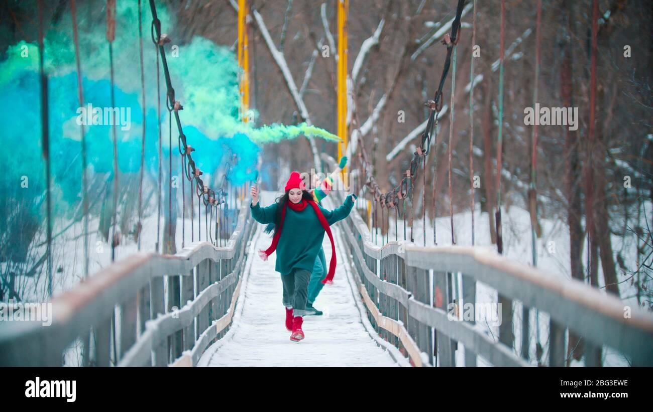 Two young women running on the snowy bridge having fun with green and ...