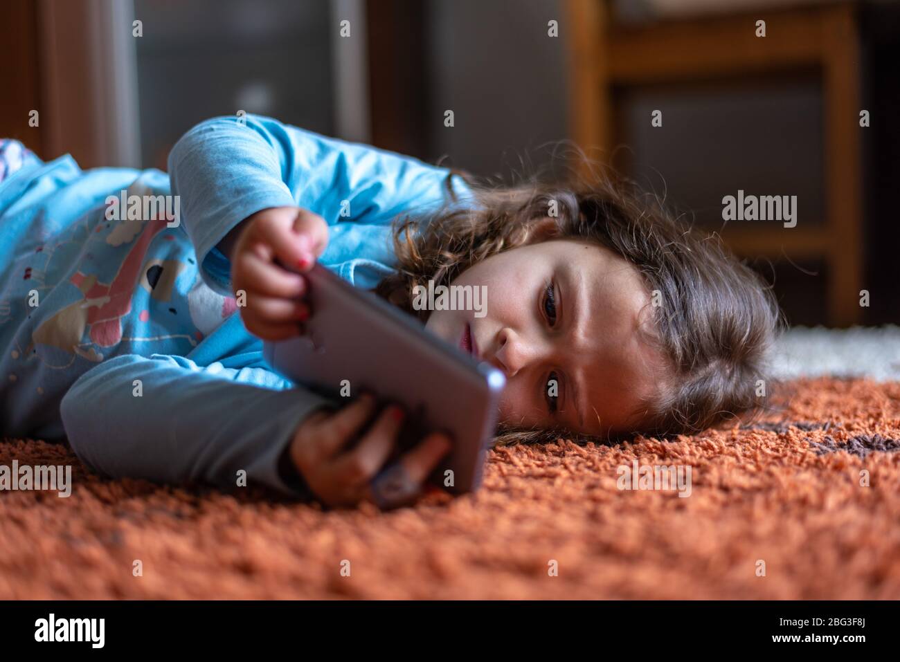 Cute little happy girl lying down on using looking digital smartphone ...