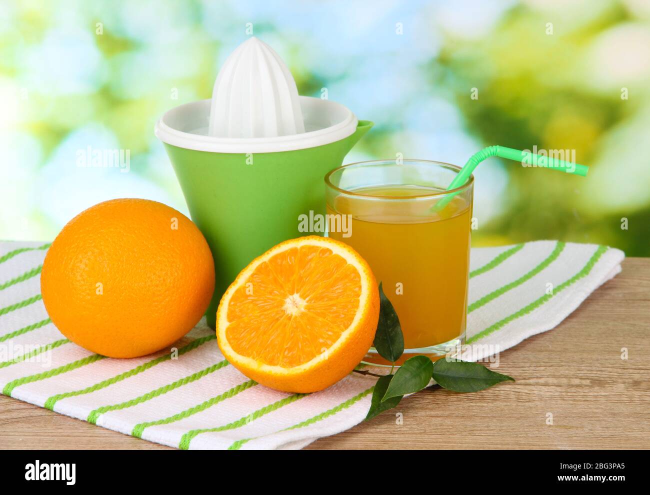Citrus press, glass of juice and ripe oranges on brown wooden table ...