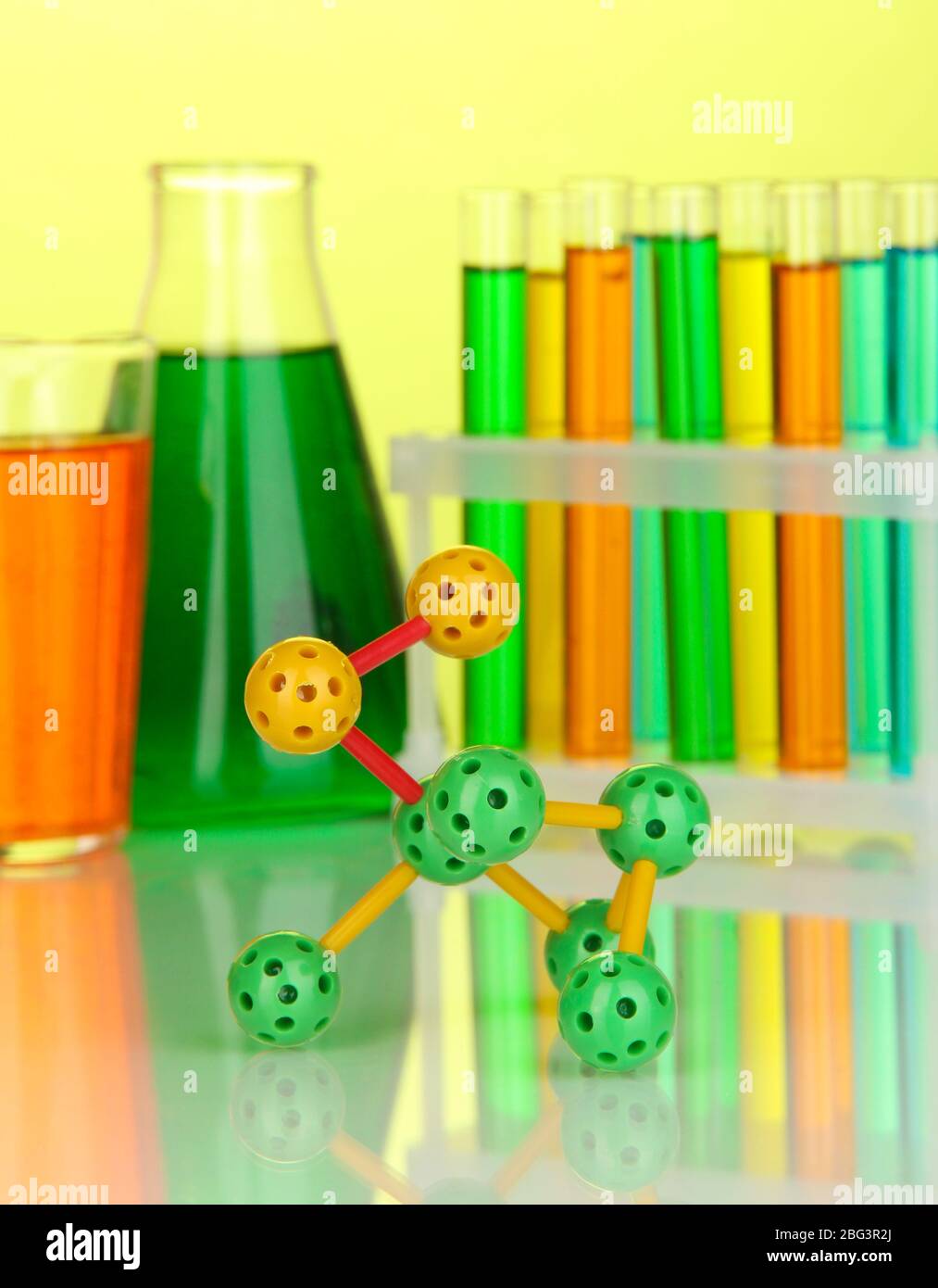 Molecule model and test tubes with colorful liquids on yellow ...