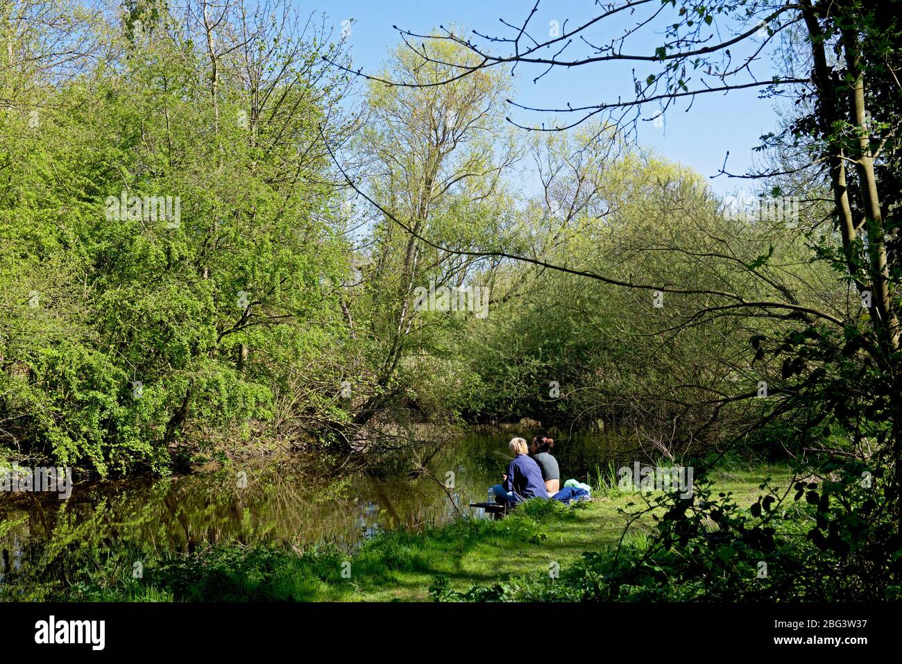 Two young women sitting by pond, Howden Marsh, a local nature reserve ...