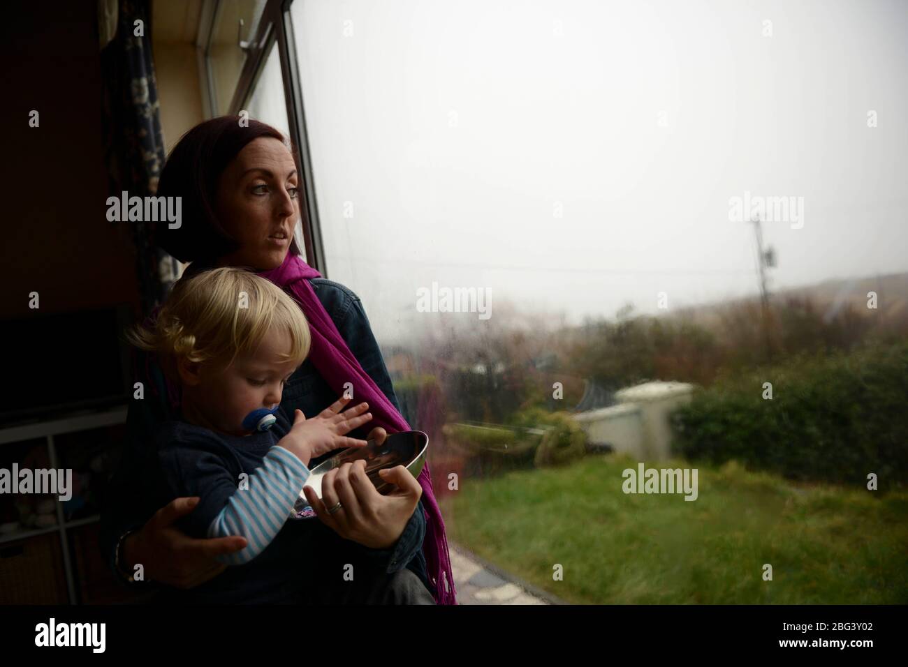 A young mother suffering from post-natal depression sits at a window ...