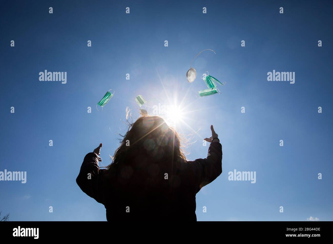 Rear view of a woman standing outdoors throwing face masks in the air ...