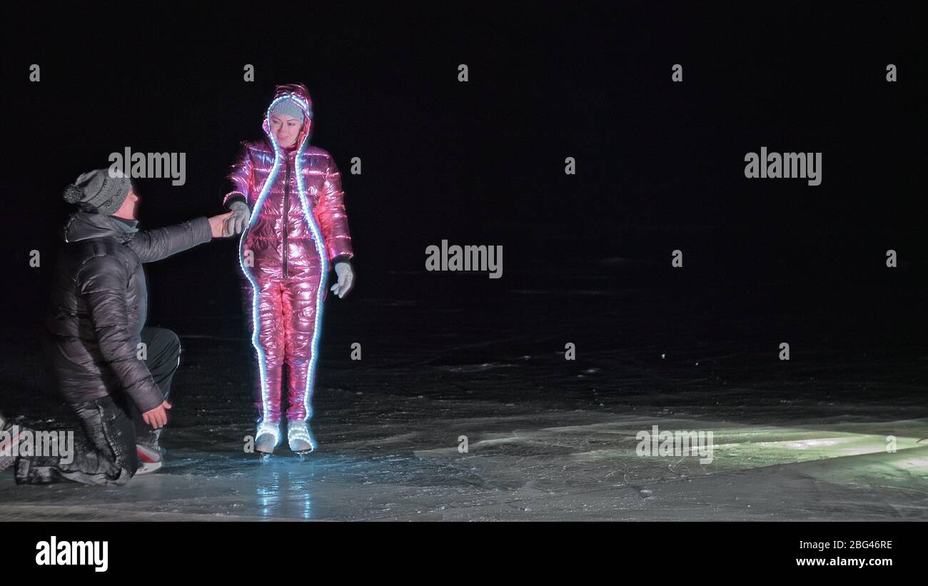 Young loving couple skating at ice rink at night. Man and woman kiss ...