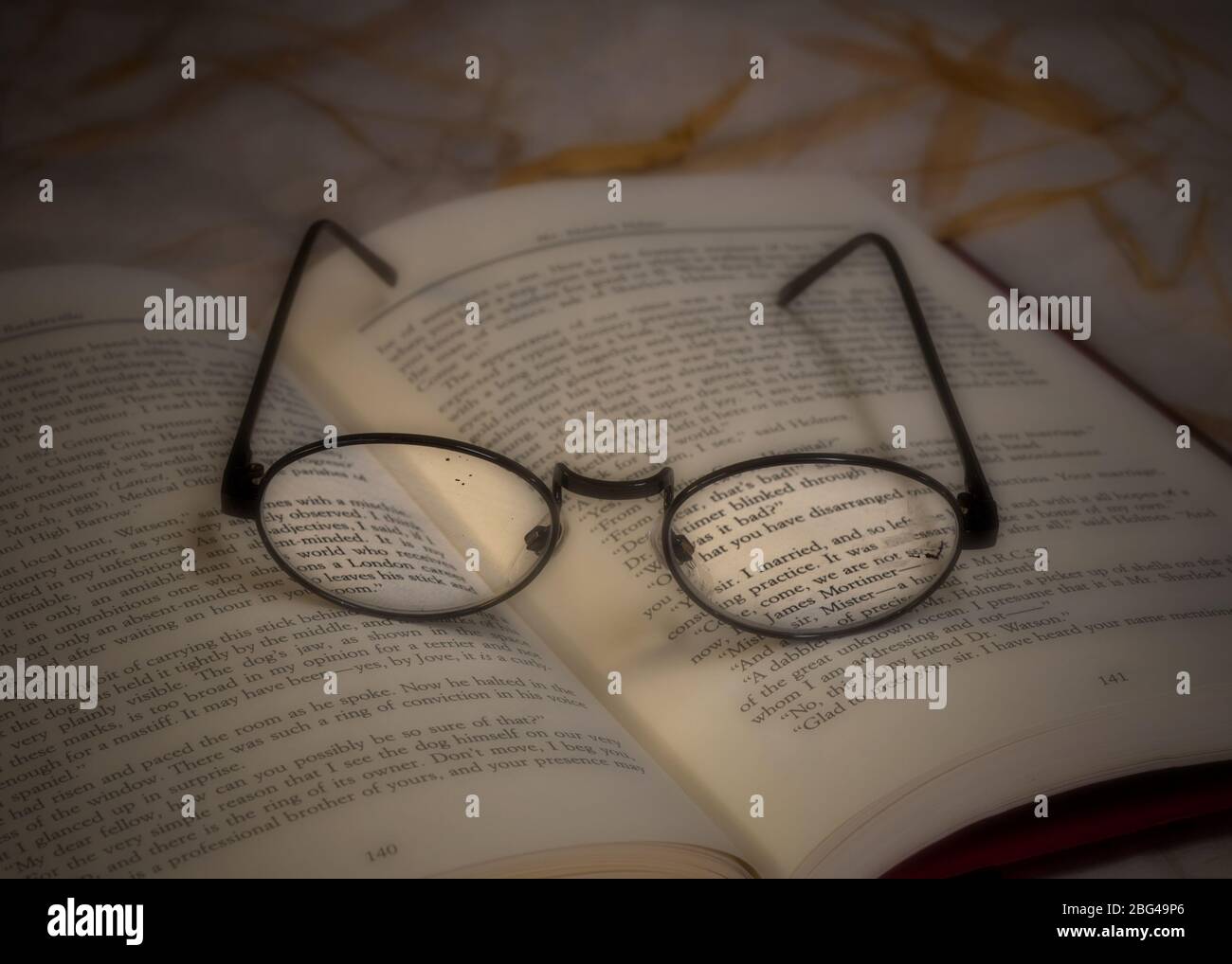 A pair of old reading glasses over an old book , angle view, croped, to ...