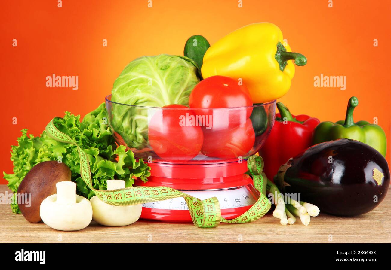 Fresh vegetables in scales on table on orange background Stock Photo ...