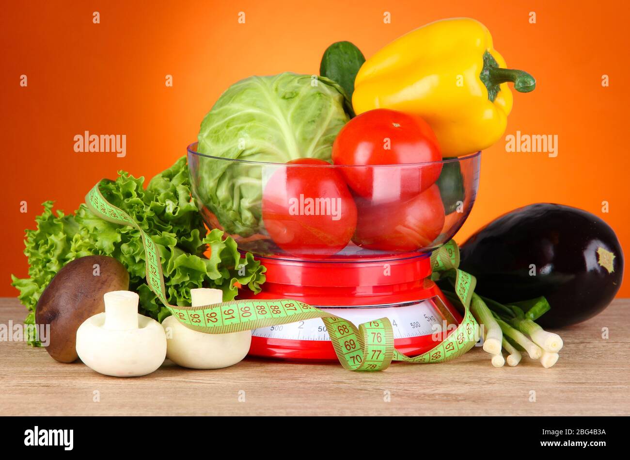 Fresh vegetables in scales on table on orange background Stock Photo ...