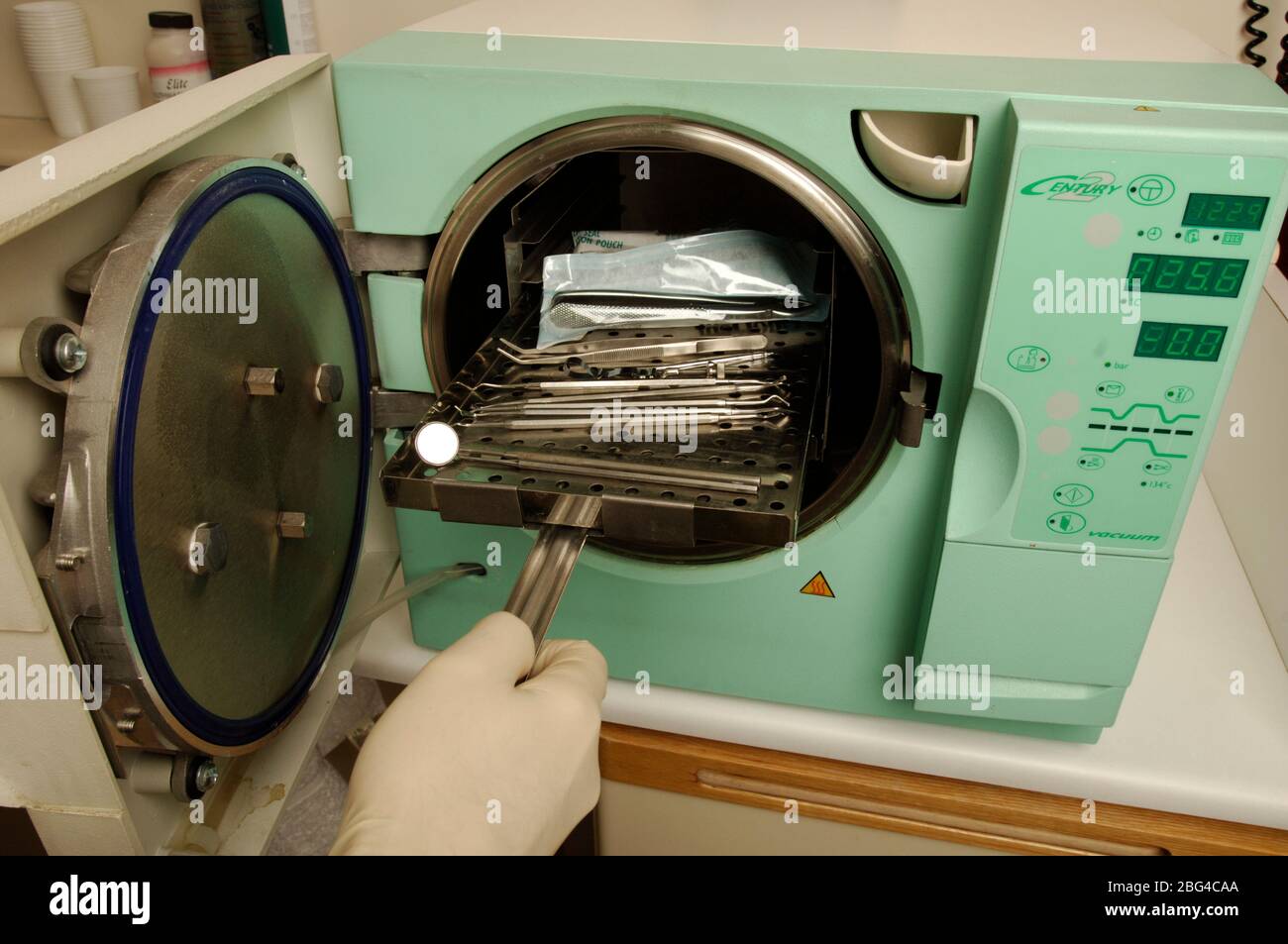 A gloved hand inserts used dental tools into an autoclave to be ...