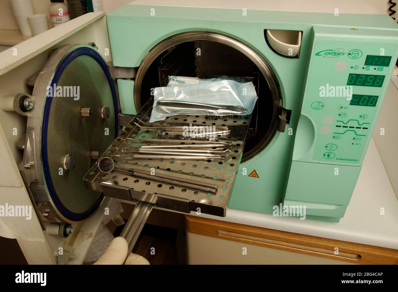 A gloved hand inserts used dental tools into an autoclave to be ...