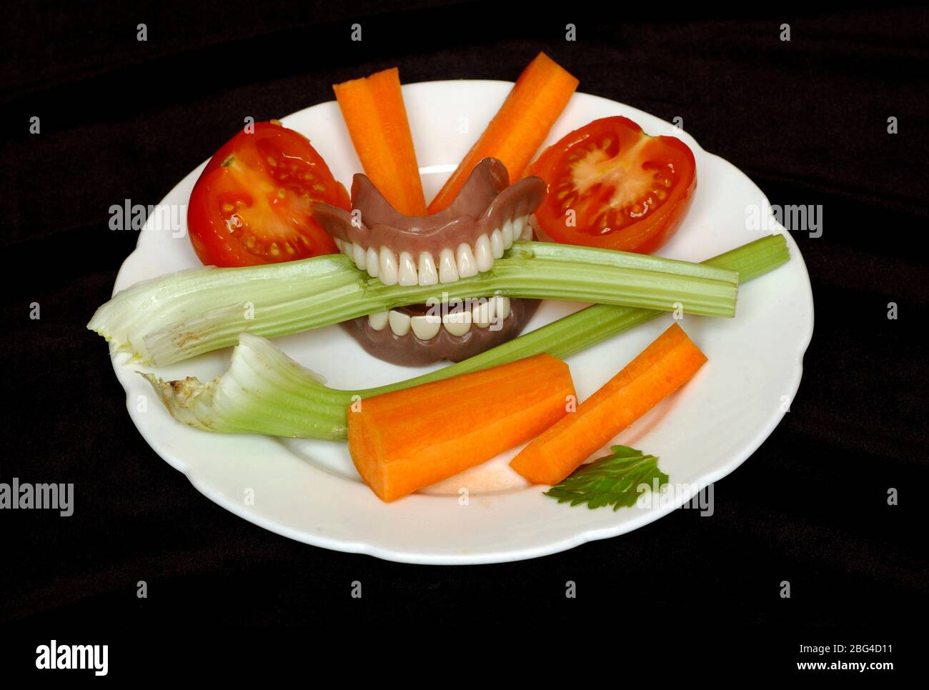 A stick of celery in between the teeth of a set of dentures, on a plate ...