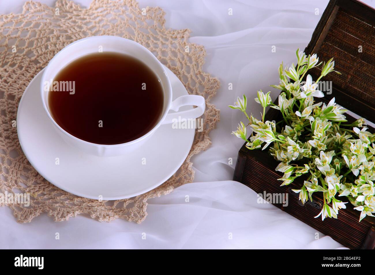 Composition with spring flowers and cup of tea on white satin ...