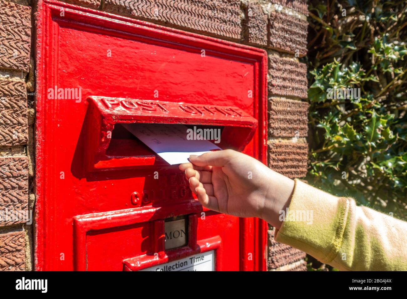 A child's hand posting a letter into a post box embedded into a brick ...