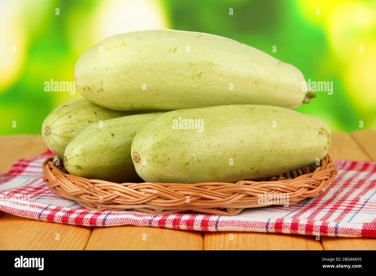Fresh marrows on wicker mat, on wooden table, on bright background ...