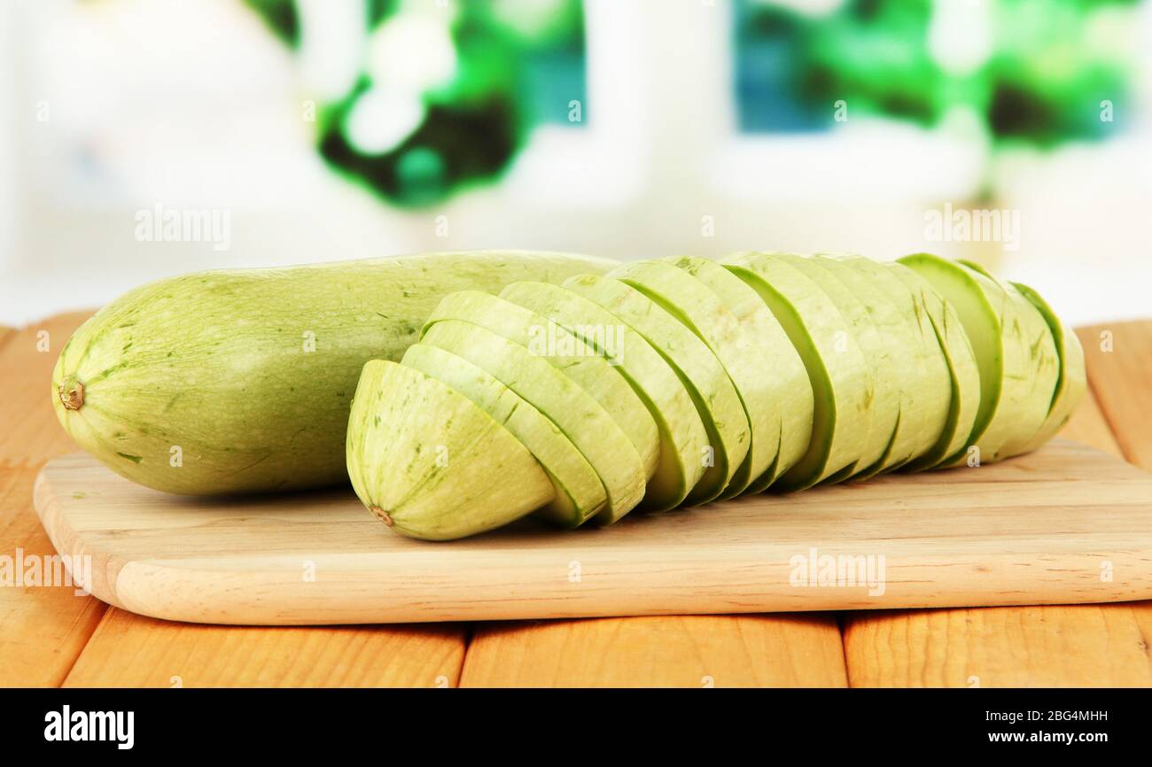 Fresh marrows on cutting board, on wooden table, on bright background ...