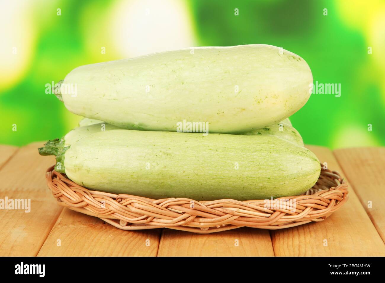 Fresh marrows on wicker mat, on wooden table, on bright background ...