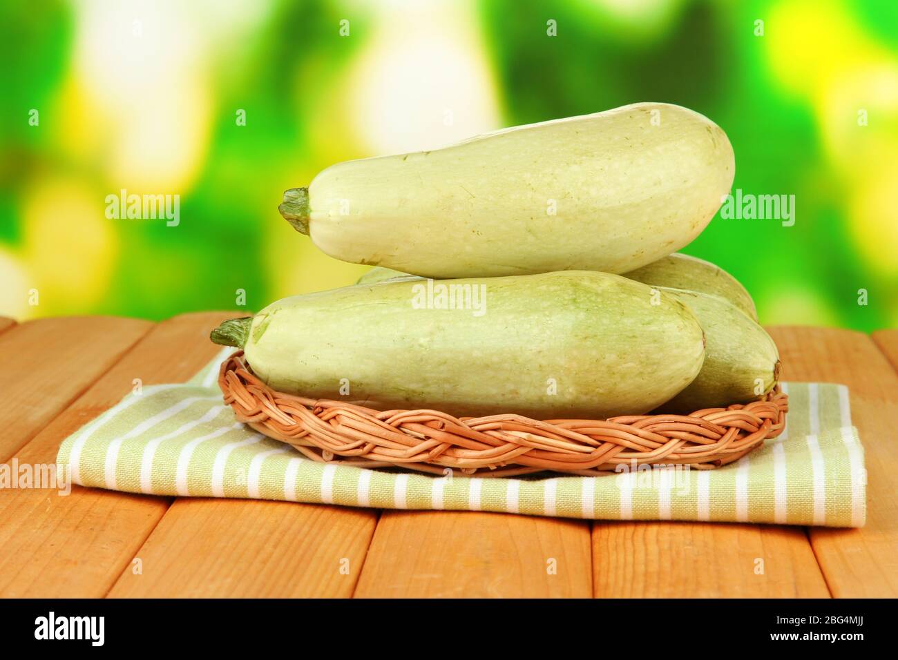 Fresh marrows on wicker mat, on wooden table, on bright background ...