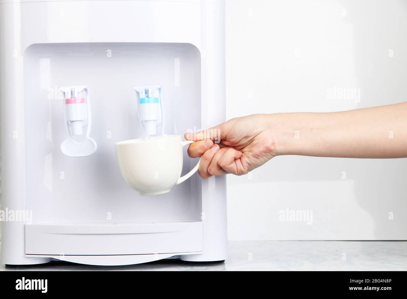 Woman filling cup at water cooler Stock Photo - Alamy