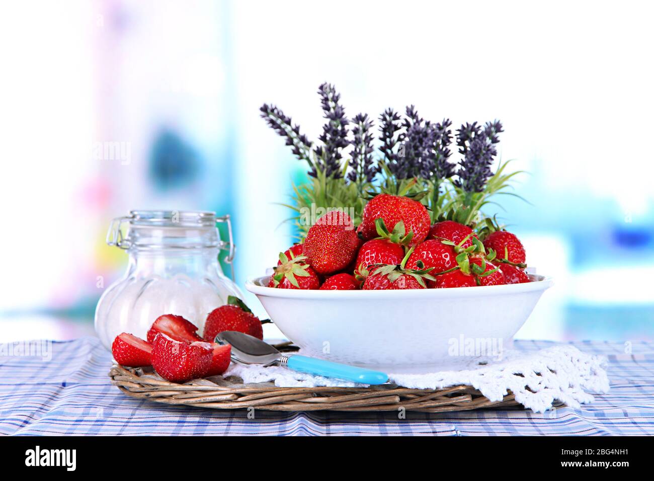 Strawberries in plate on wicker stand on table on window background ...