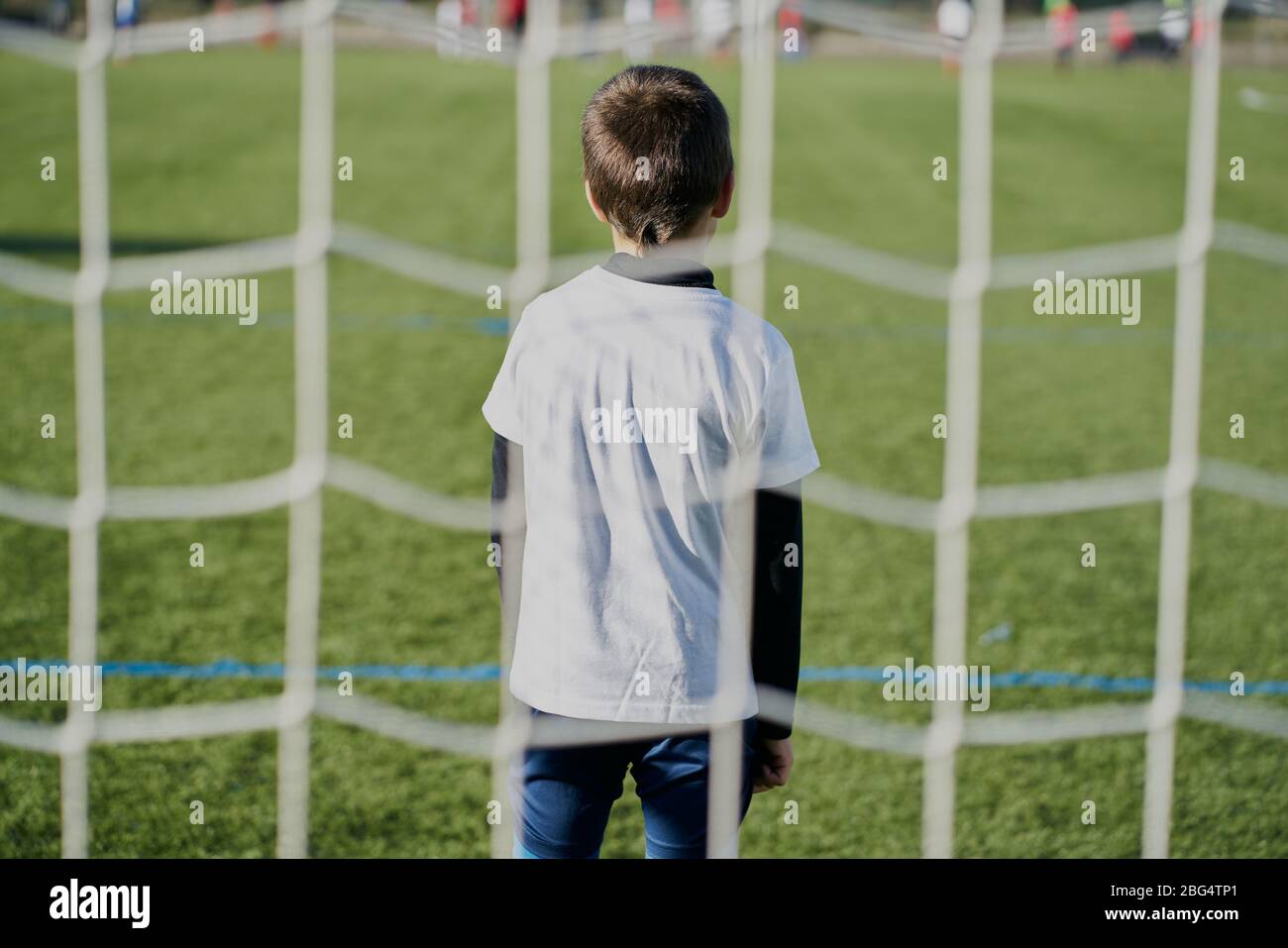 Rear view behind the net of a child football goalkeeper in the goal ...