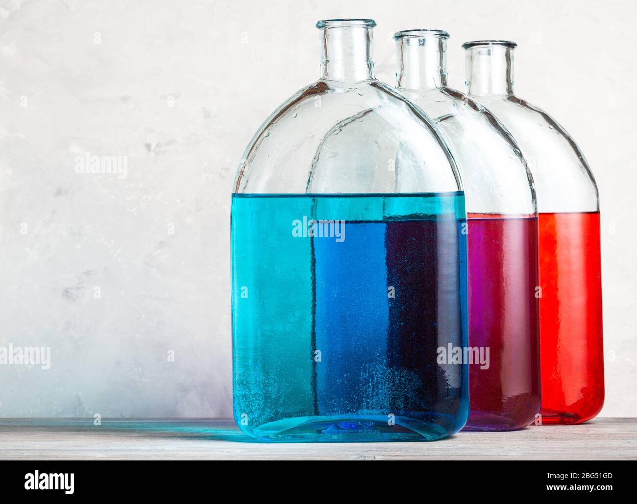 glass flasks with color ink solutions on gray wooden board near gray ...