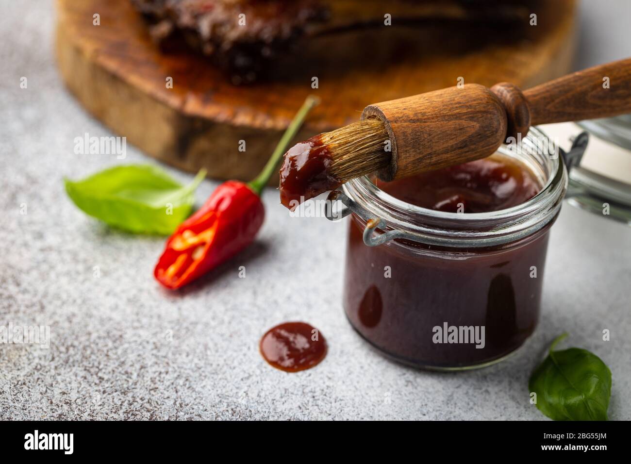 Barbecue sauce in glass jar with basting brush over gray stone table ...