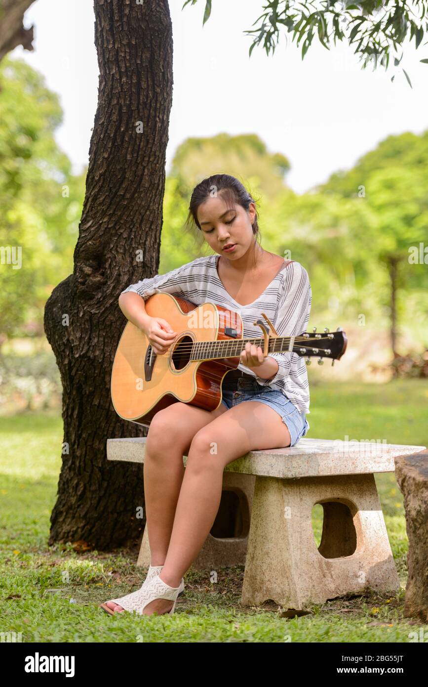 Full body shot of young Asian woman playing guitar at the park Stock ...