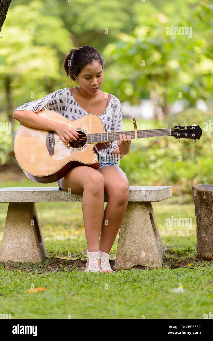 Full body shot of young Asian woman playing guitar at the park Stock ...