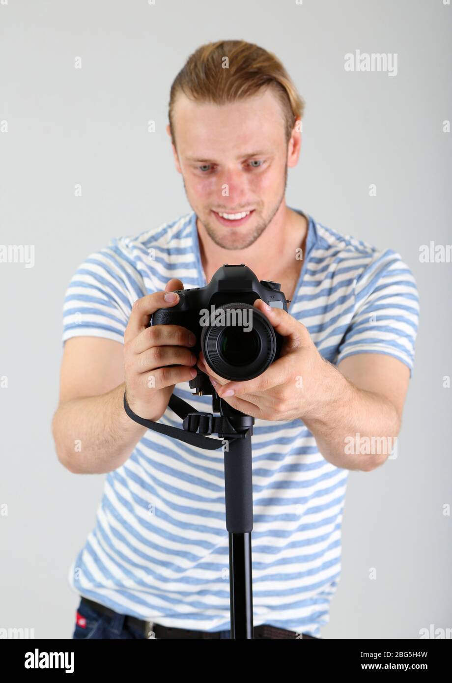 Handsome photographer with camera on monopod, on gray background Stock ...