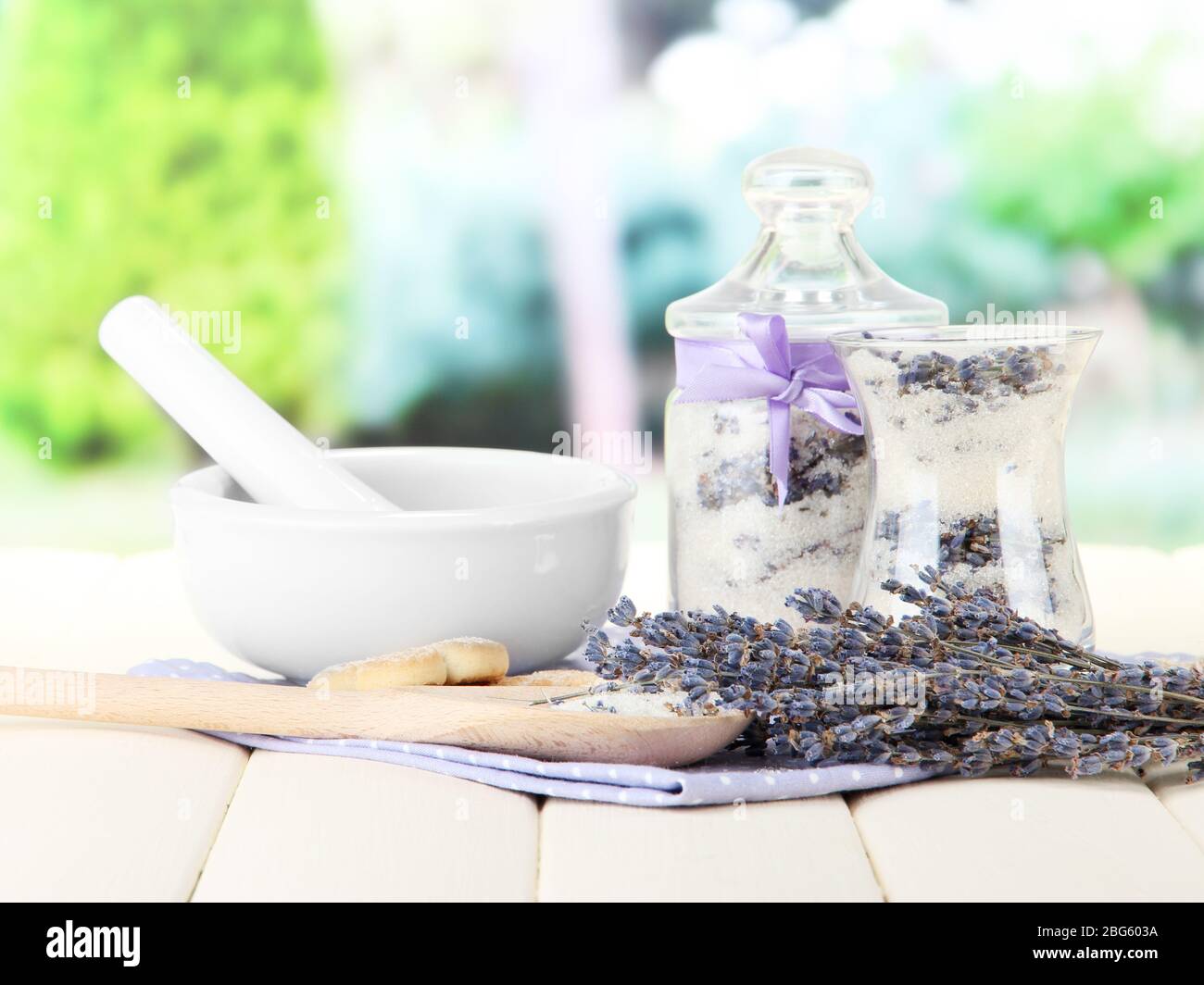 Still life with jar of lavender sugar, mortar and fresh lavender flowers on bright background ...