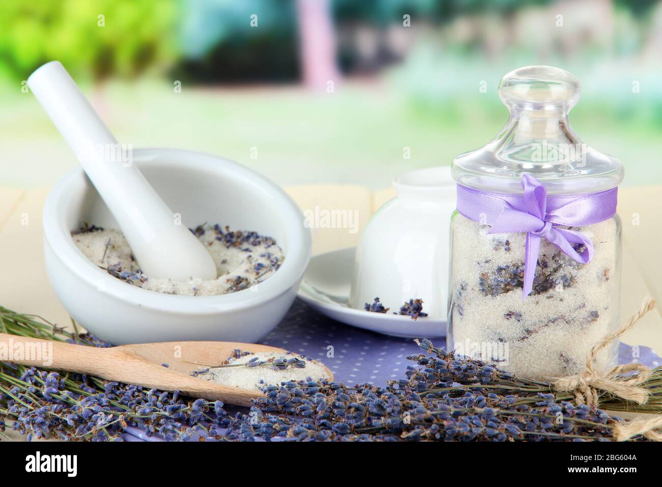 Still life with jar of lavender sugar, mortar and fresh lavender flowers on bright background ...