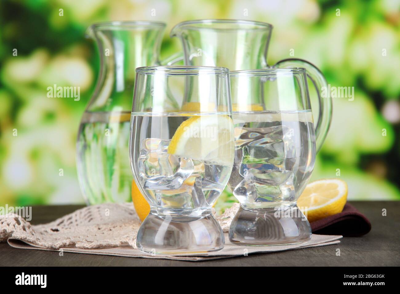 Glass pitchers of water and glasses on wooden table on natural ...