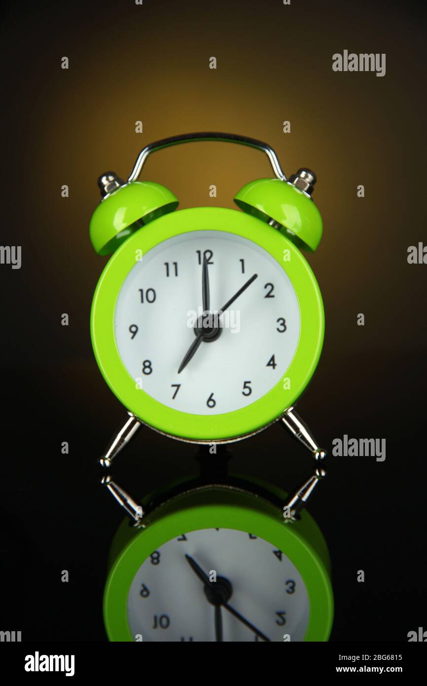 Green alarm clock on dark yellow background Stock Photo - Alamy