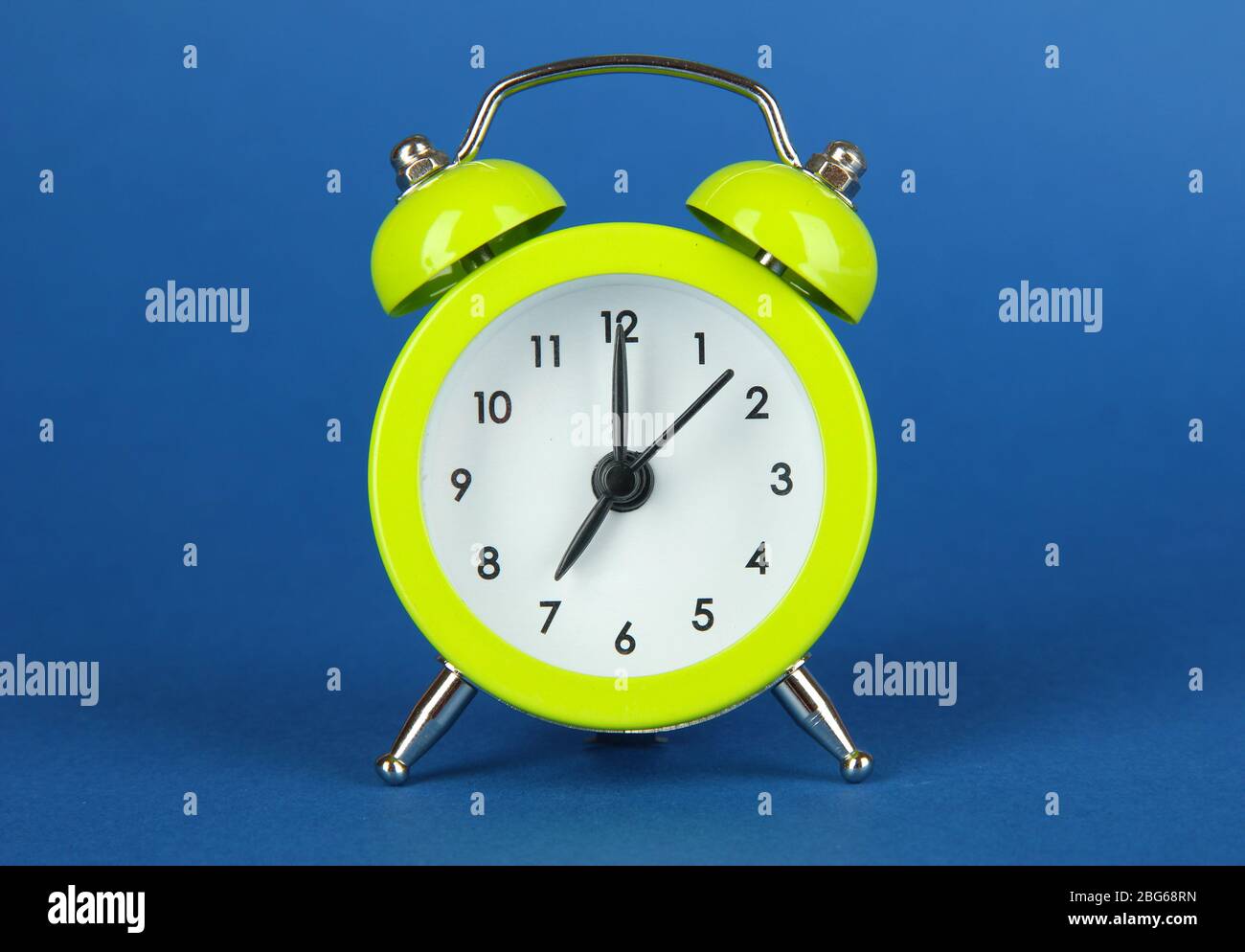 Green alarm clock on blue background Stock Photo - Alamy