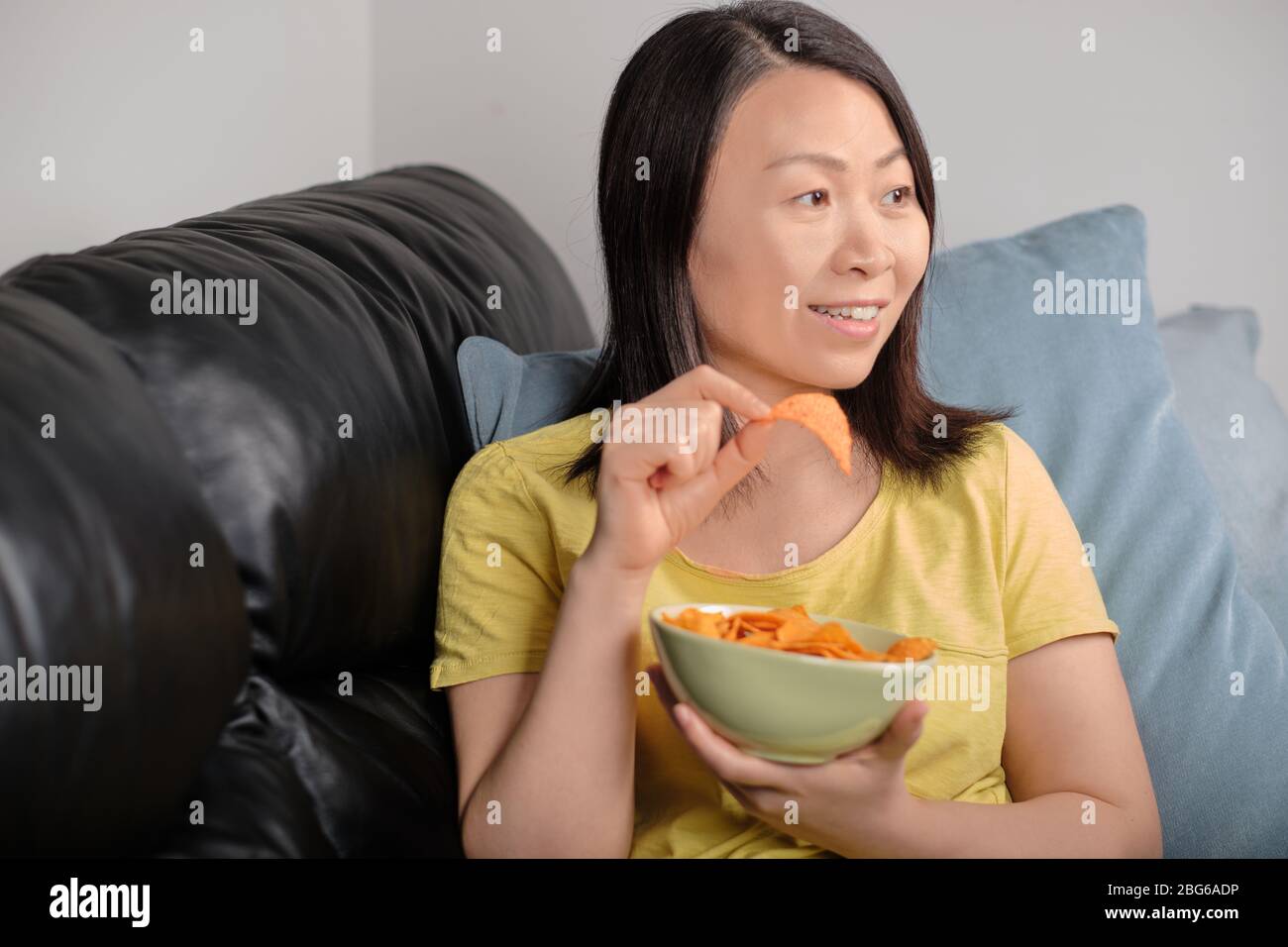 Beautiful asian woman sitting down, smiling and relaxing at home eating ...