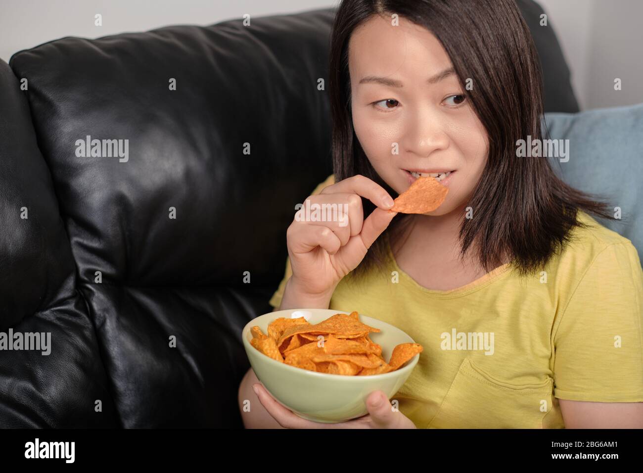 Beautiful asian woman sitting down, smiling and relaxing at home eating ...