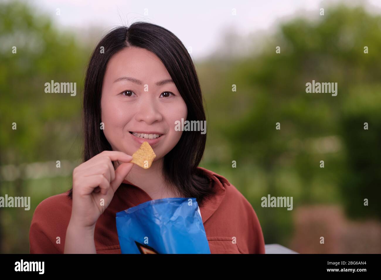 Beautiful asian woman standing on balcony smiling and eating doritos ...