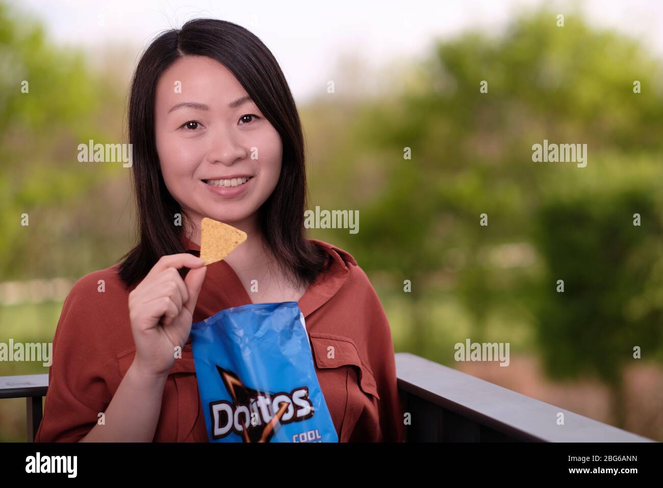 Beautiful asian woman standing on balcony smiling and eating doritos ...