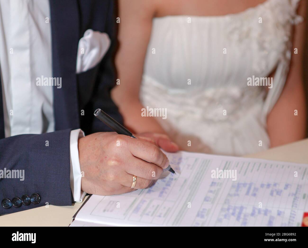 The groom puts her signature in the marriage document, selective focus ...