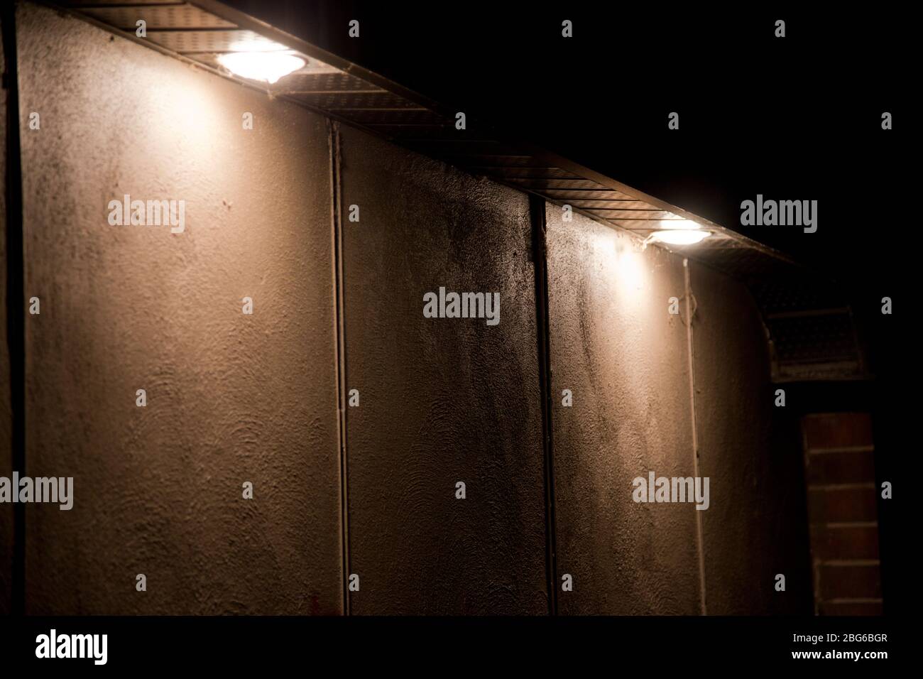 Two large pot lights illuminating a concrete wall in the dark ...