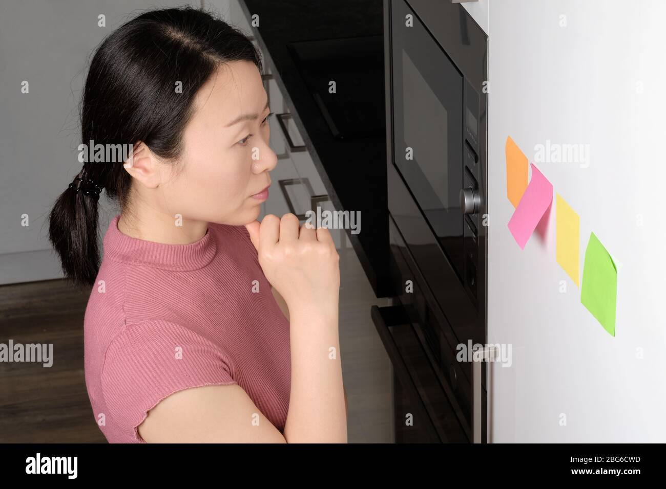 Oriental young woman reading multicolored generic reminder notes stuck ...