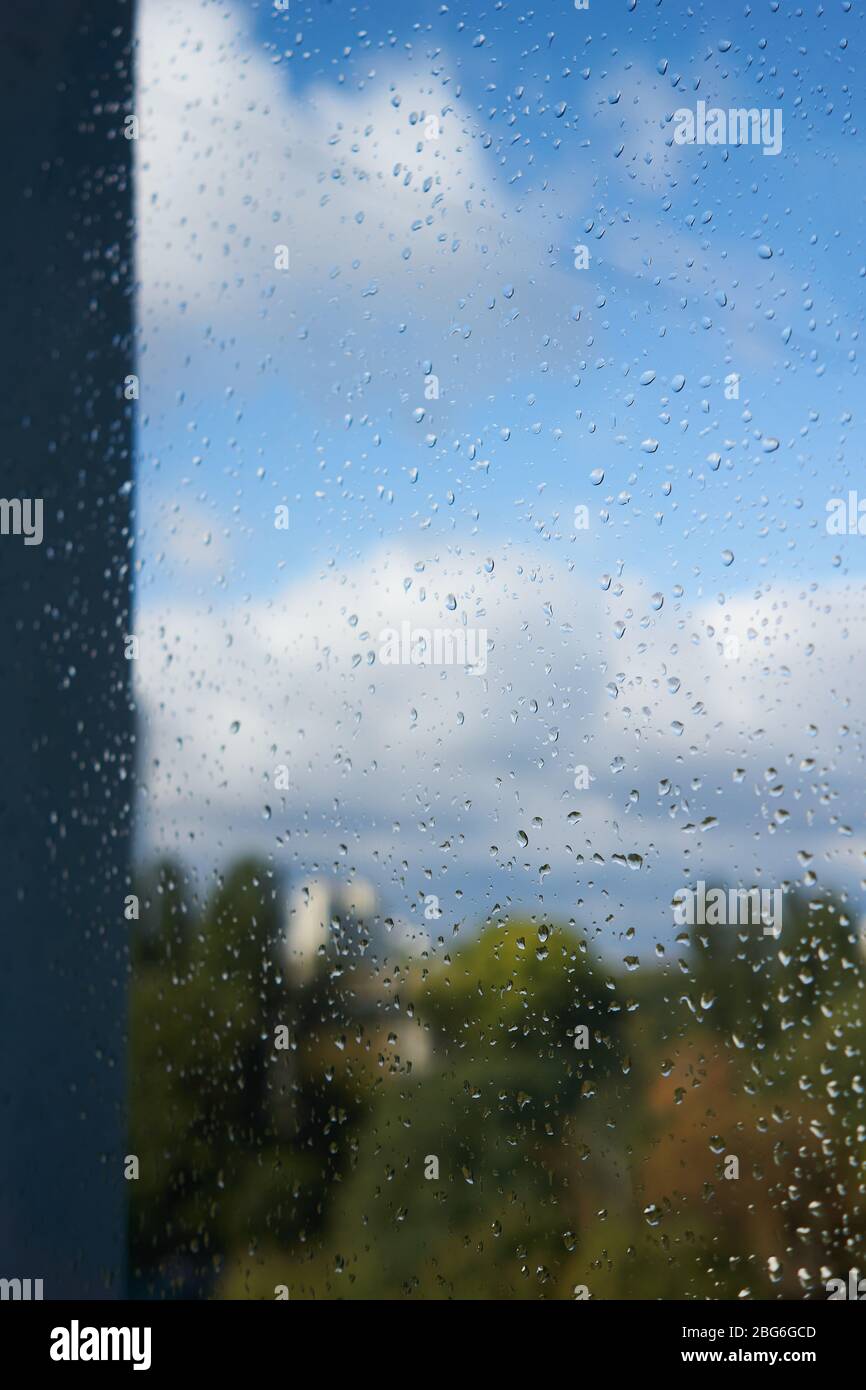 Water drops on a window in front of the blue sky with green trees ...